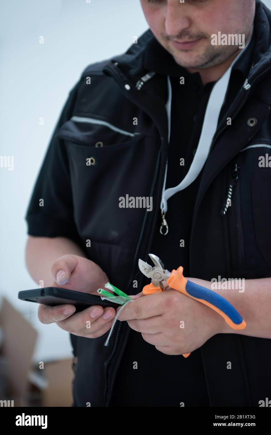 electrical engineer with wire and pliers in his hand using mobile phone ...