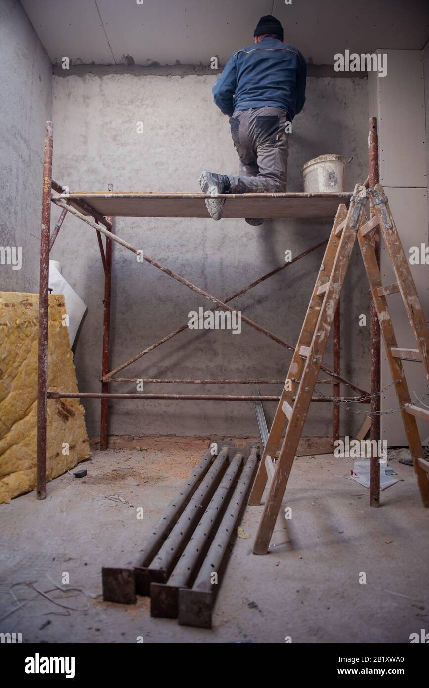 young professional construction worker using scaffold while plastering ...