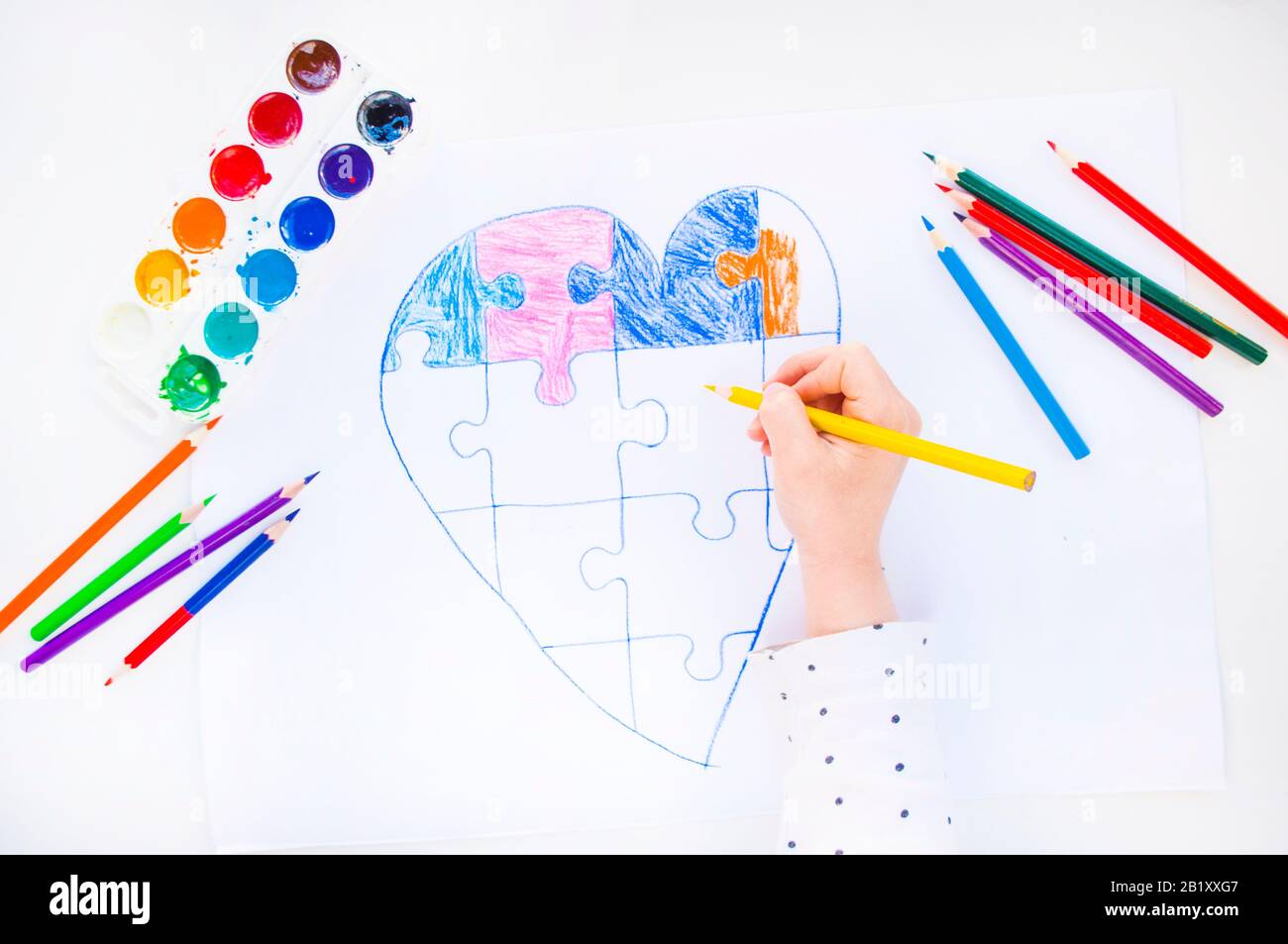 A child is drawing colorful heart with jigsaw puzzle on white ...