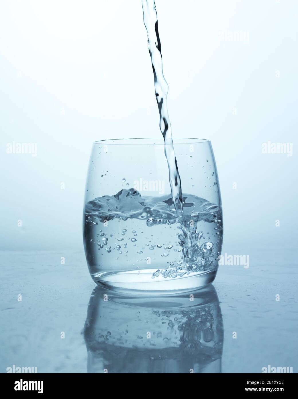 Water jet falling into a glass with splashes and drops, air bubbles ...