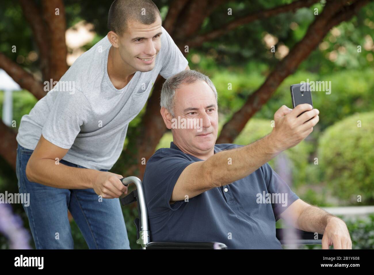man in wheelchair taking selfie with young man pushing chair Stock ...