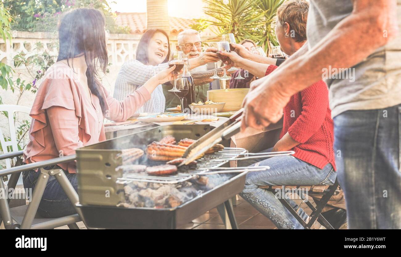 Family and friends cheering with wine, grilling meat for at bbq meal ...