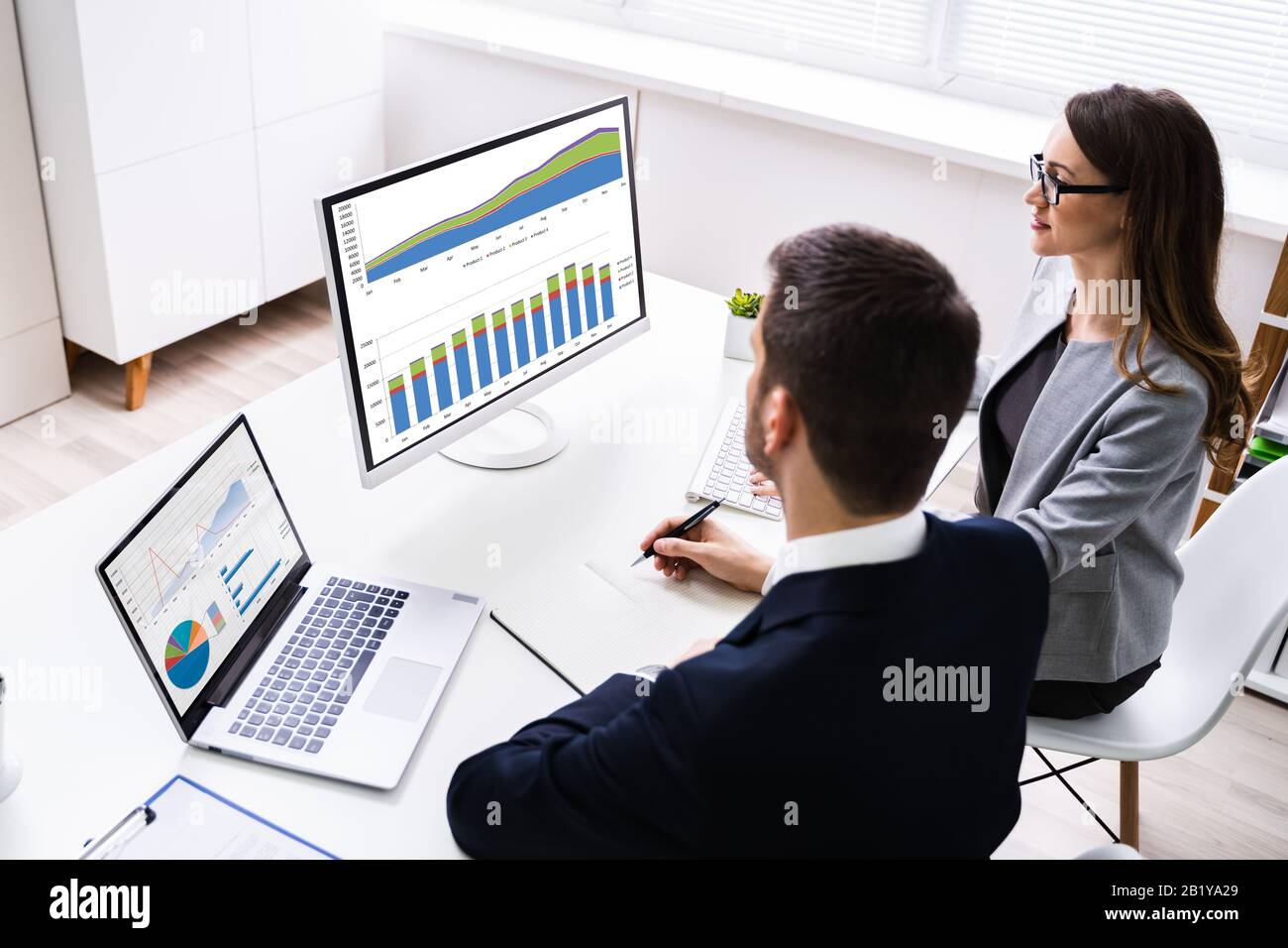 Two Businesspeople Examining Graph On Computer At Workplace Stock Photo ...