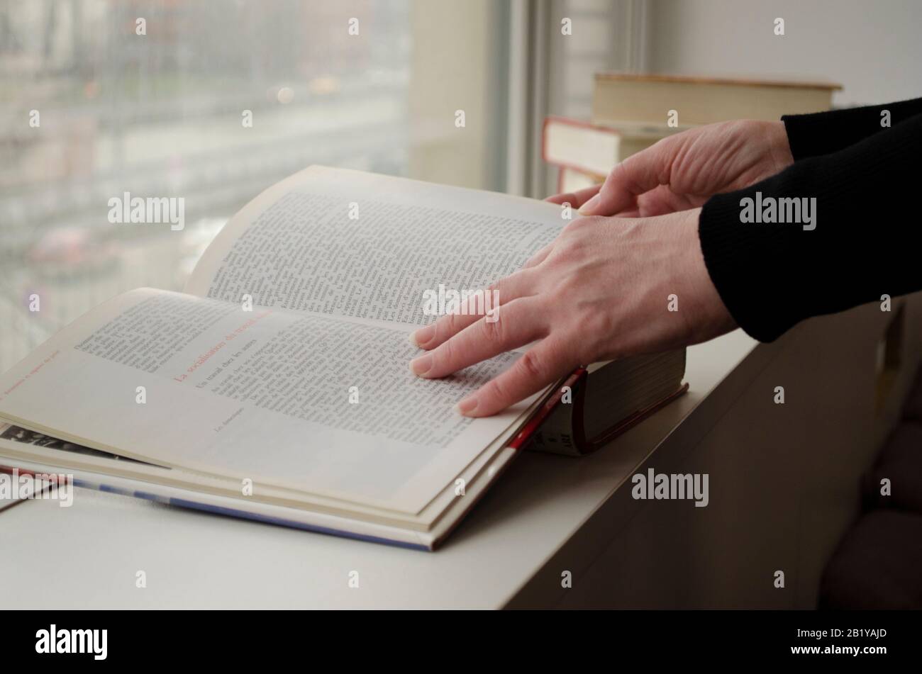 A person reading books near the window. Hands turns over book page ...