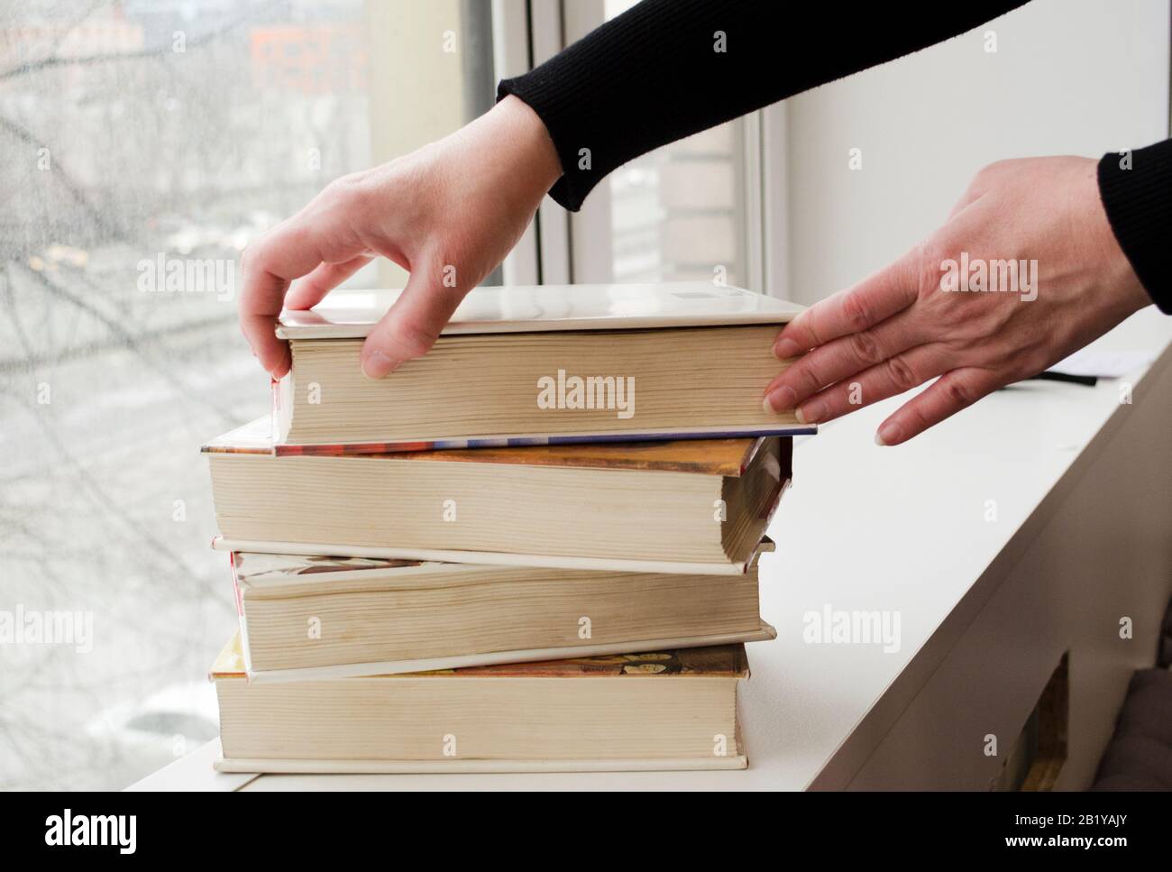 A person reading books near the window. Hands turns over book page ...
