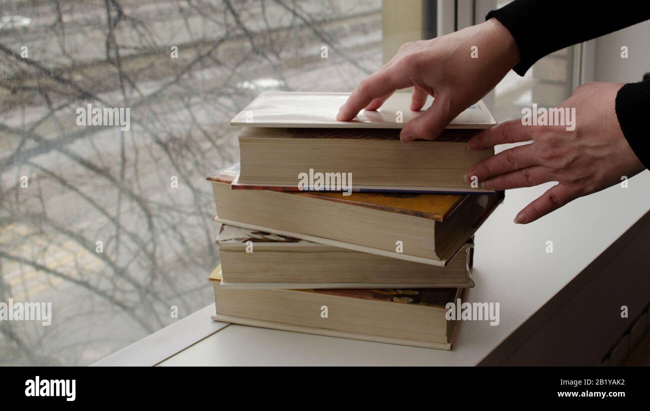 A person reading books near the window. Hands turns over book page ...