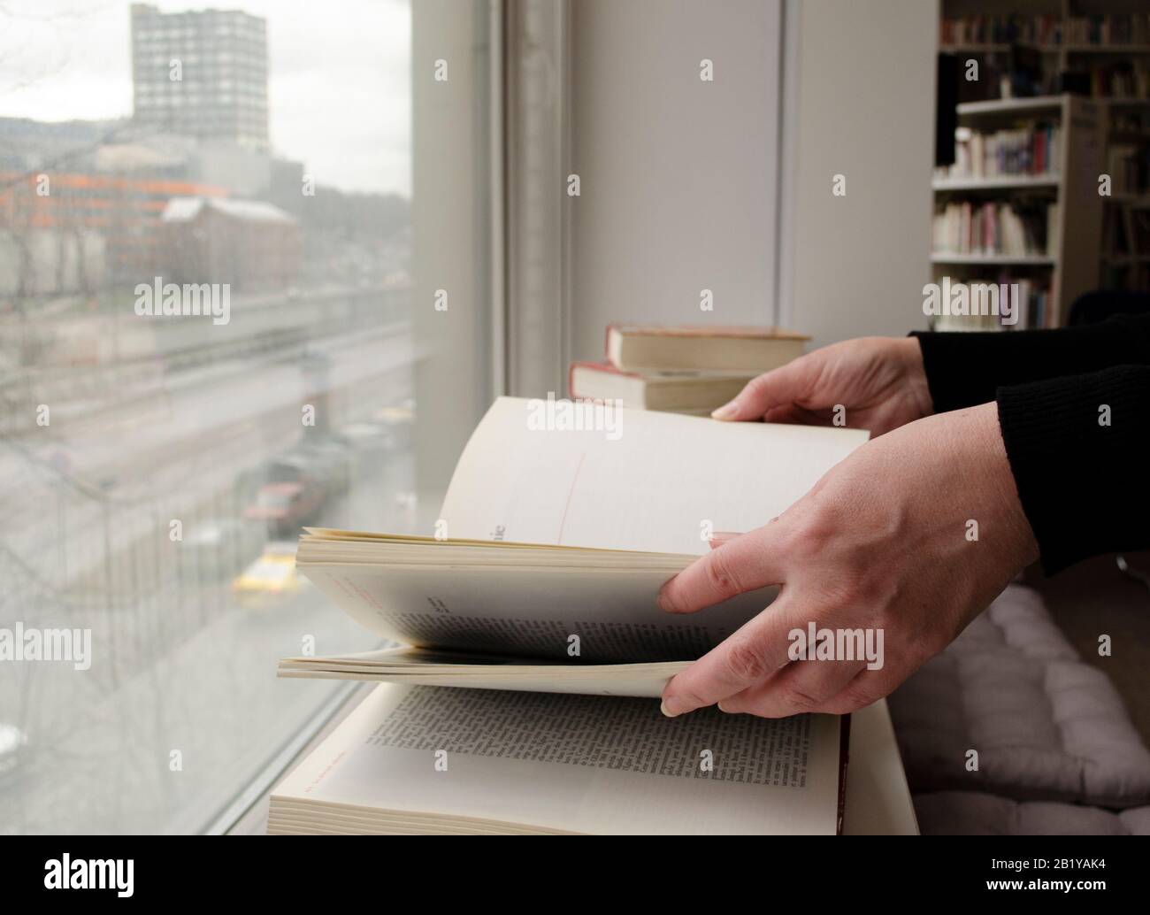 A person reading books near the window. Hands turns over book page ...