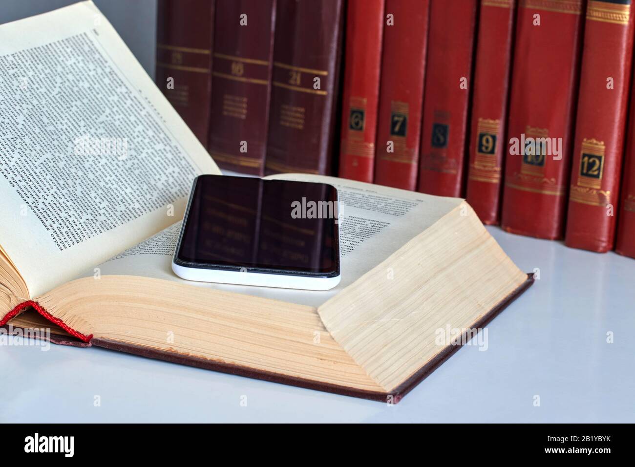 phone on an open old book on a white table on a background of books ...