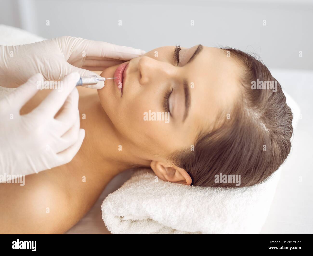 Beautician doing beauty procedure with syringe to face of young brunette woman. Cosmetic ...