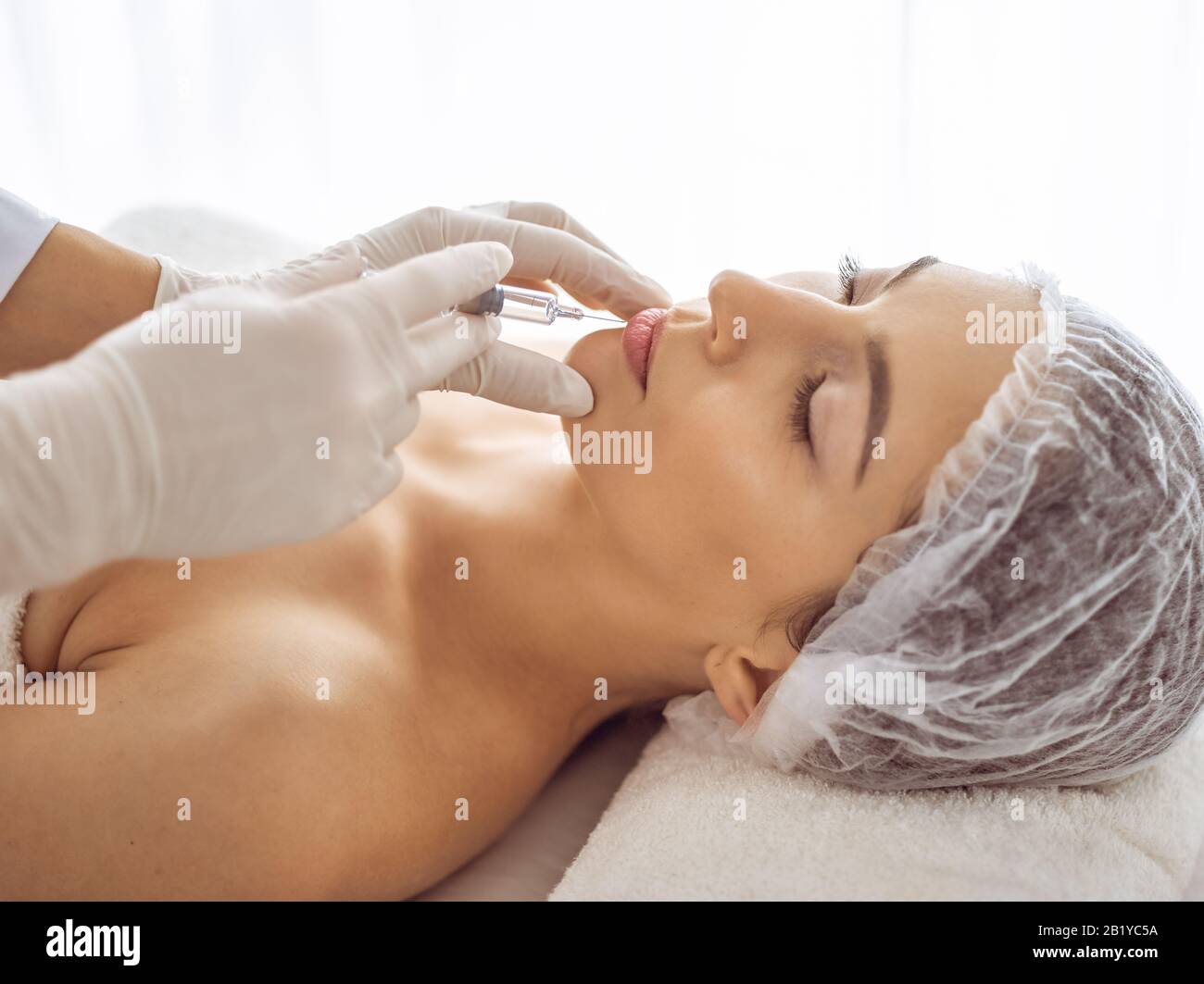Beautician doing beauty procedure with syringe to face of young brunette woman. Cosmetic ...