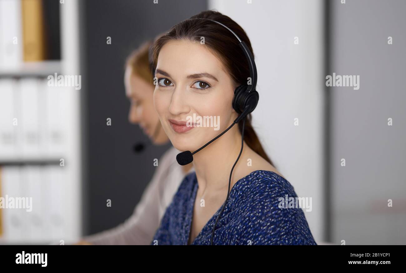 Latin american businesswoman talking by headset while sitting in office ...