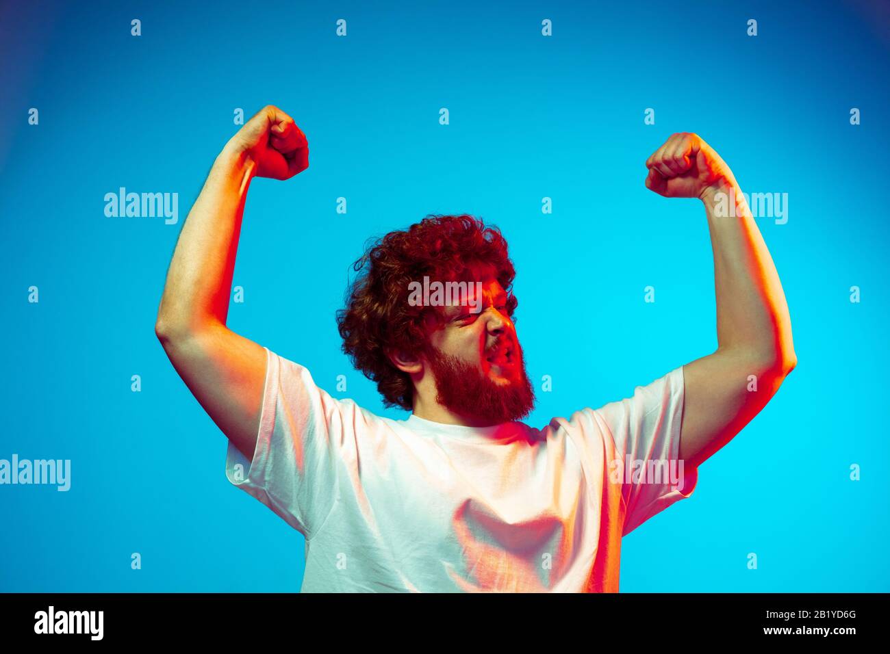 Winning, crazy happy. Caucasian man's portrait isolated on blue studio ...