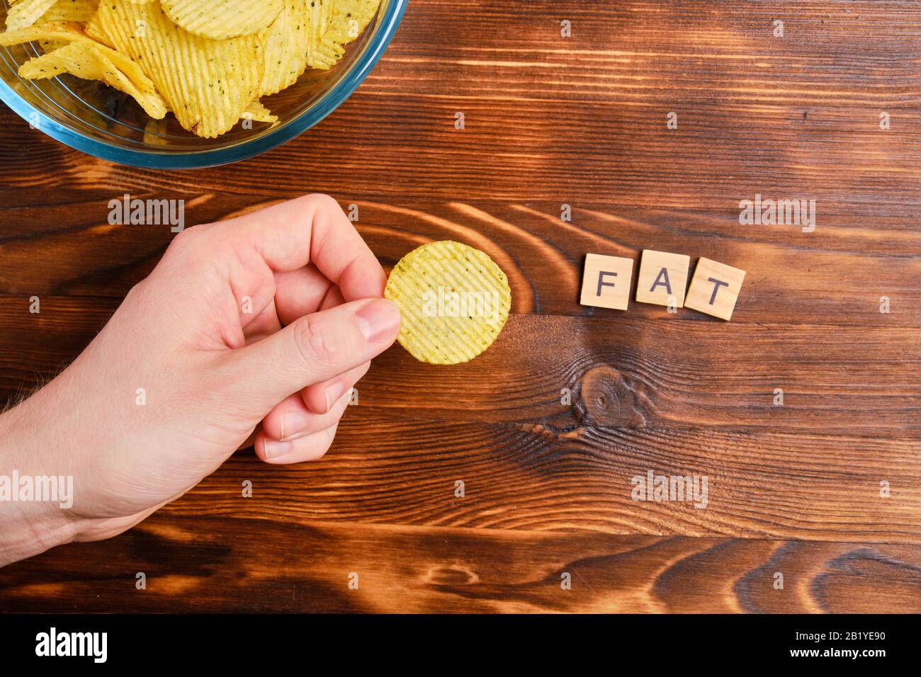Hand holding chips on a wooden background with the word fat on wooden ...