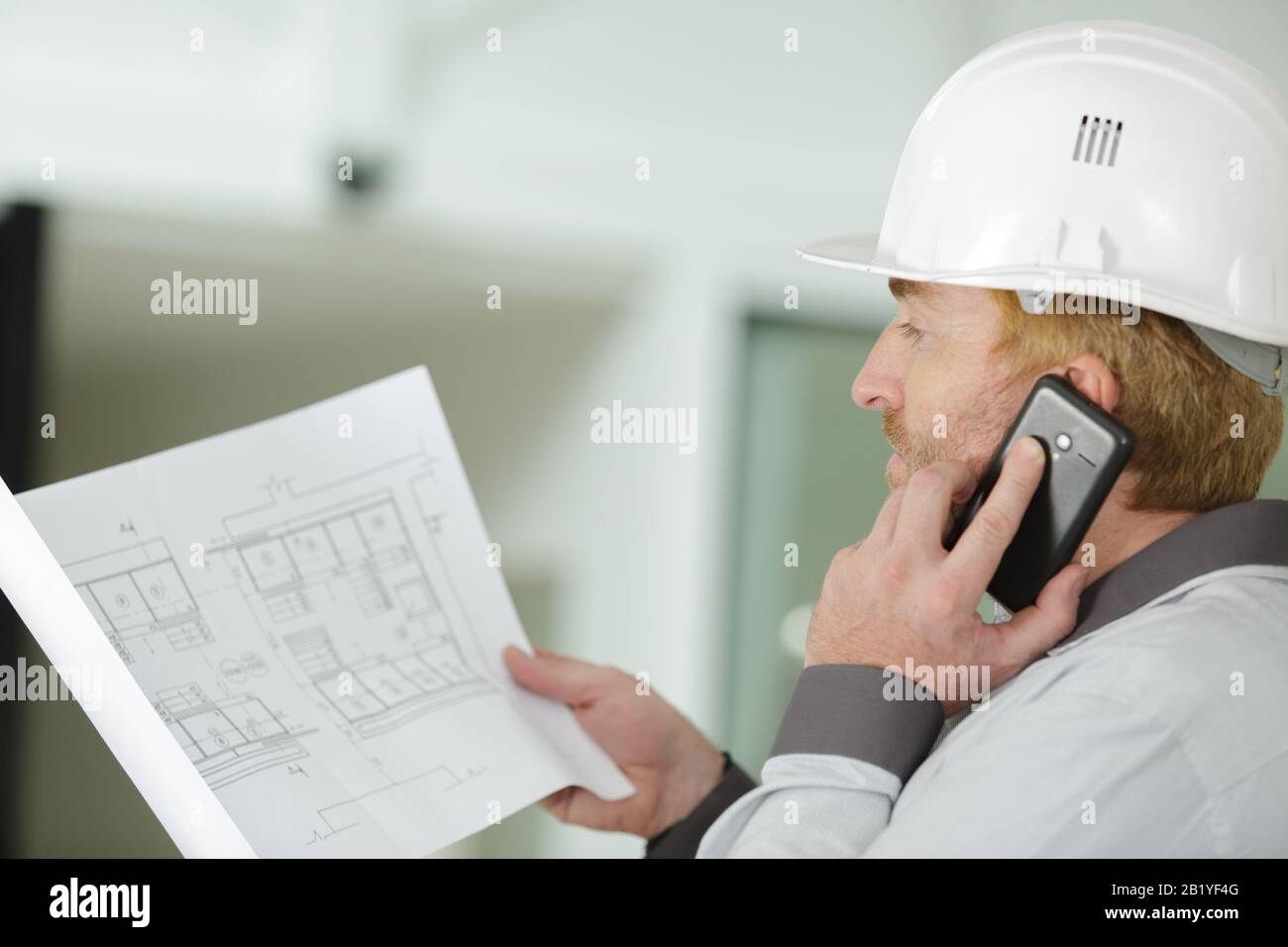 worker examines drawing and talks on a mobile phone Stock Photo - Alamy