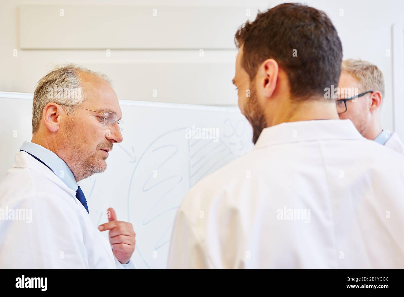Doctors presenting around the meeting stand around a whiteboard Stock ...