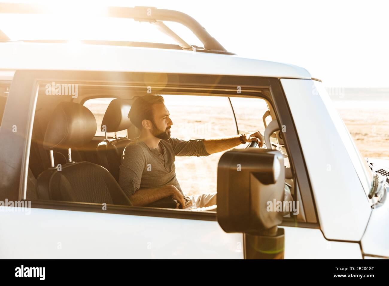 Image of handsome serious young man drive the car outdoors at the beach ...
