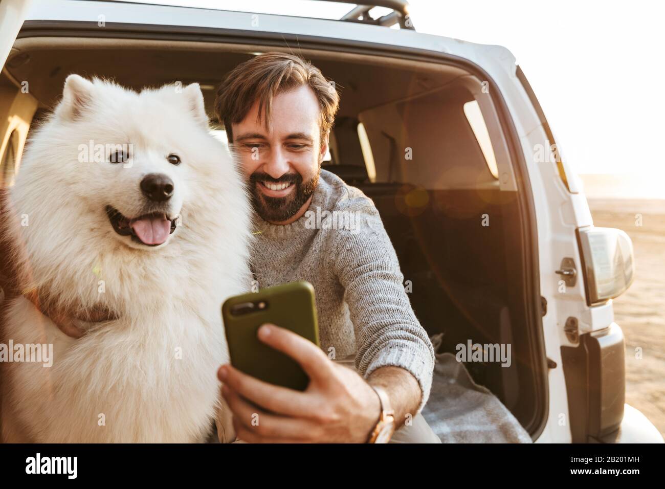 Image of smiling young man with dog samoyed outdoors at the beach in ...