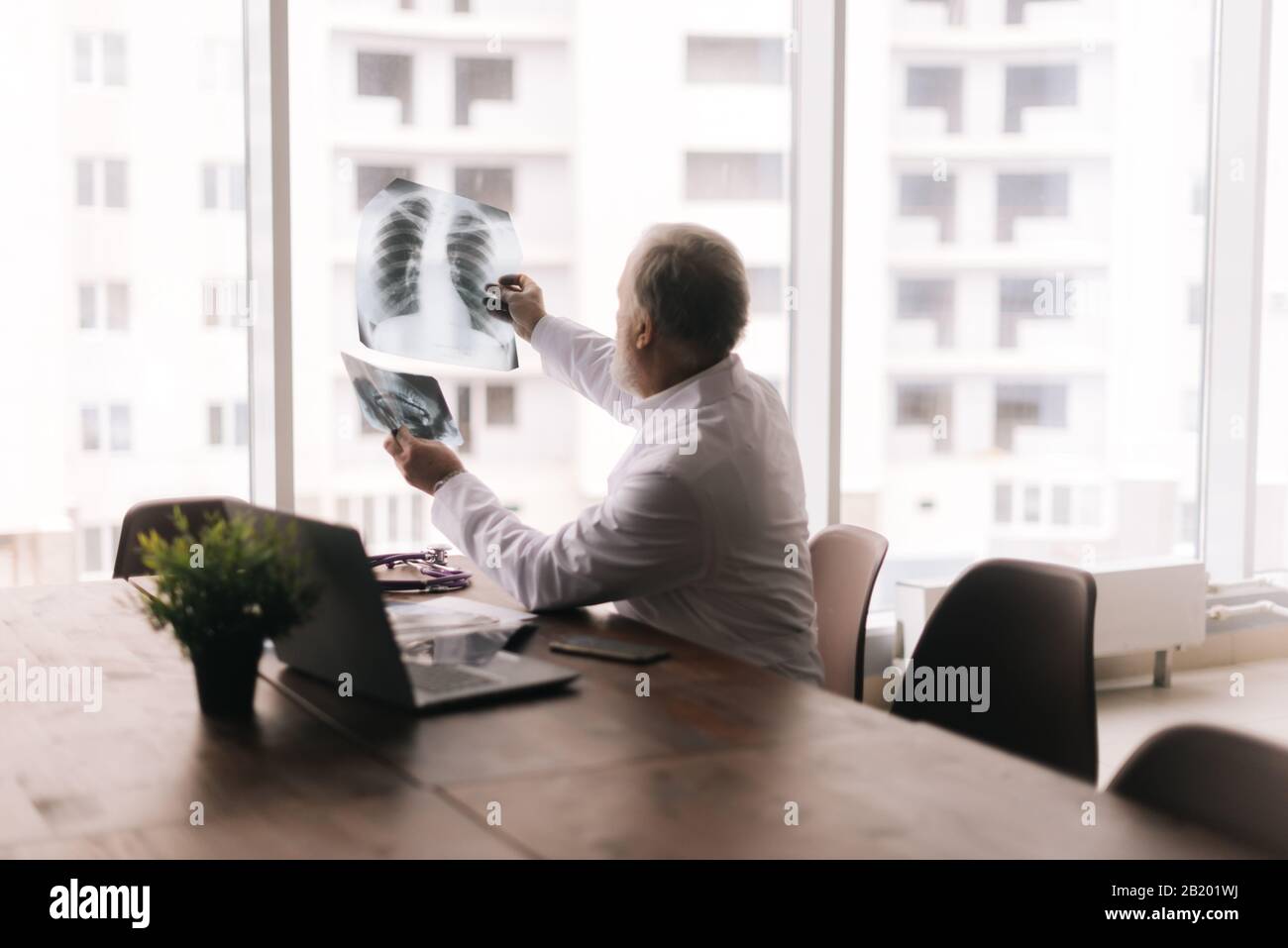 Adult male doctor examining x-ray and MRI scan at a table against large ...