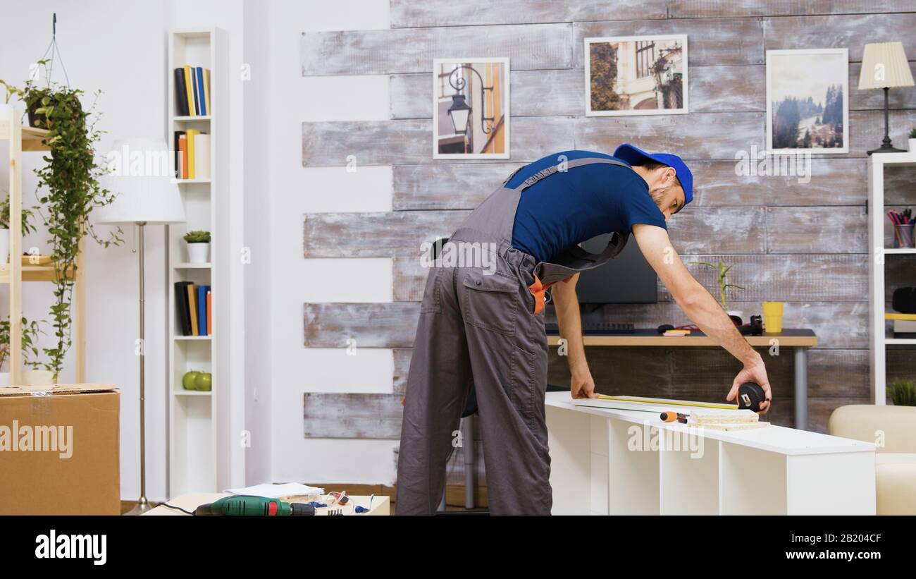 Furniture assembly worker standing reading instruction and using a tape ...