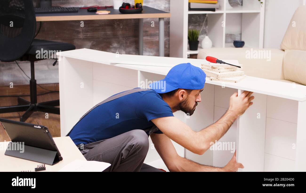 Attractive handyman assembles new furniture for home owners. Worker ...