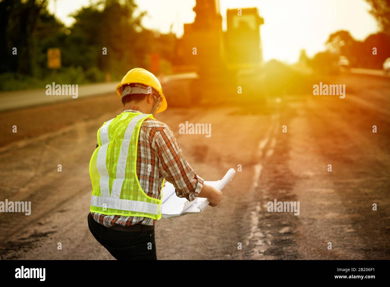 Engineer holding blueprint with backhoe background Stock Photo - Alamy