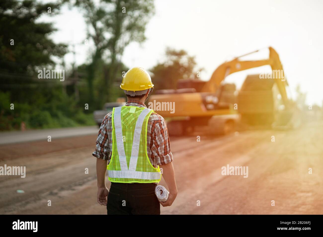 Engineer holding blueprint with backhoe background Stock Photo - Alamy