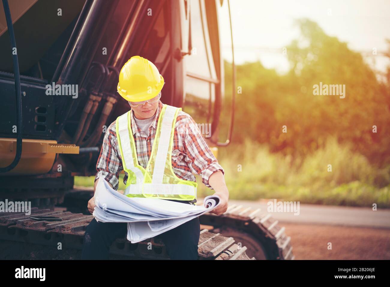 Engineer holding blueprint with backhoe background Stock Photo - Alamy