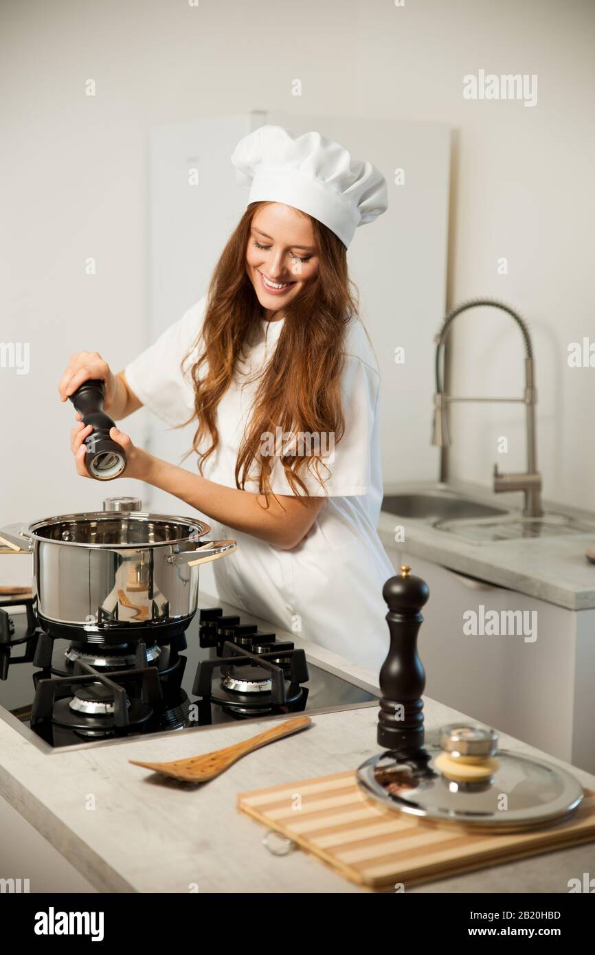 Beautiful young woman in white chef uniform cooking in the kitchen ...