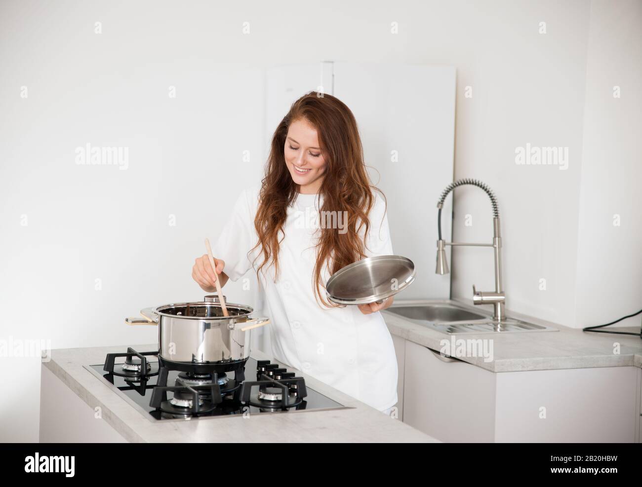 Beautiful young woman in white chef uniform cooking in the kitchen ...