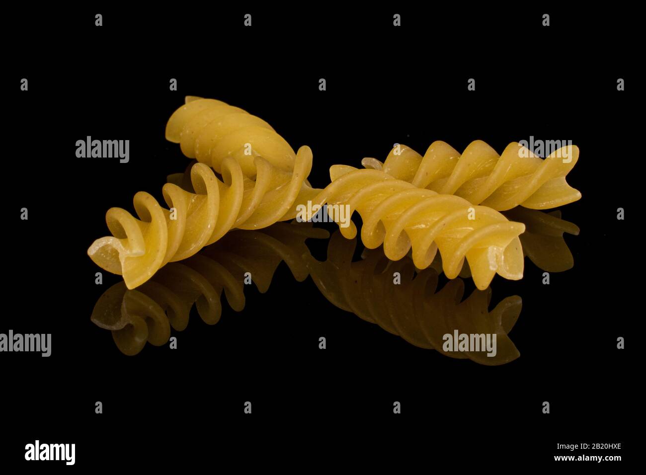 Group of four whole small yellow pasta fusilli isolated on black glass ...