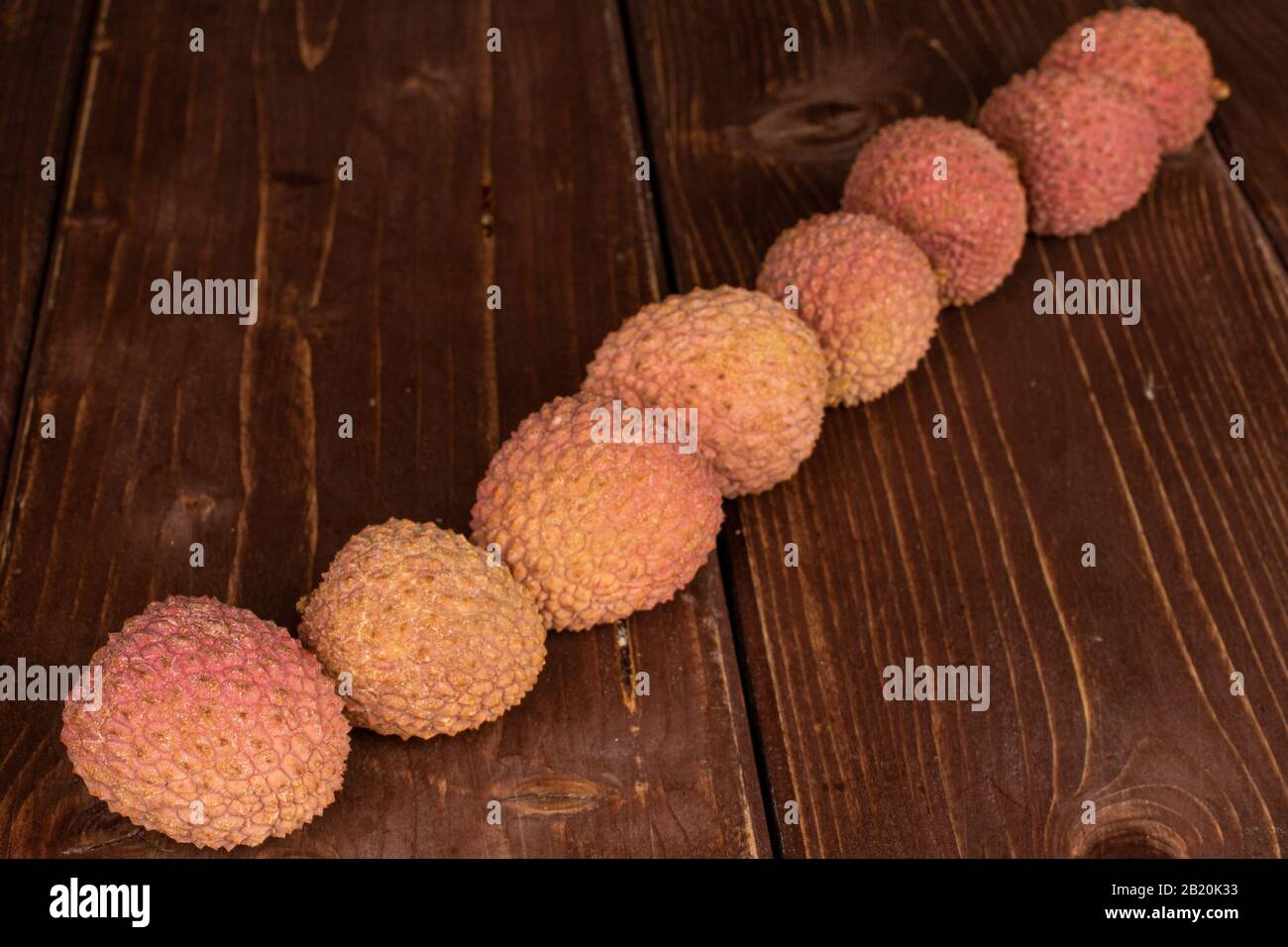Group of eight whole fresh lychee on brown wood Stock Photo - Alamy
