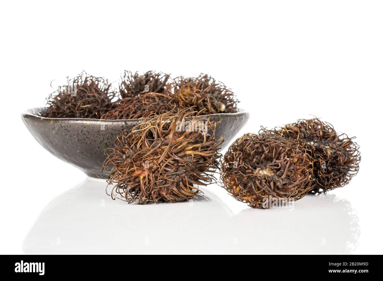 Lot of whole old brown rambutan in glazed bowl isolated on white ...