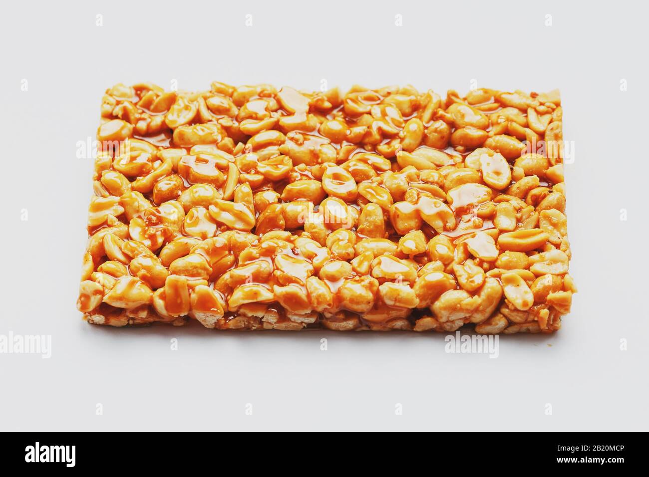 A large tile of roasted peanuts bar in a sweet molasses on a white ...
