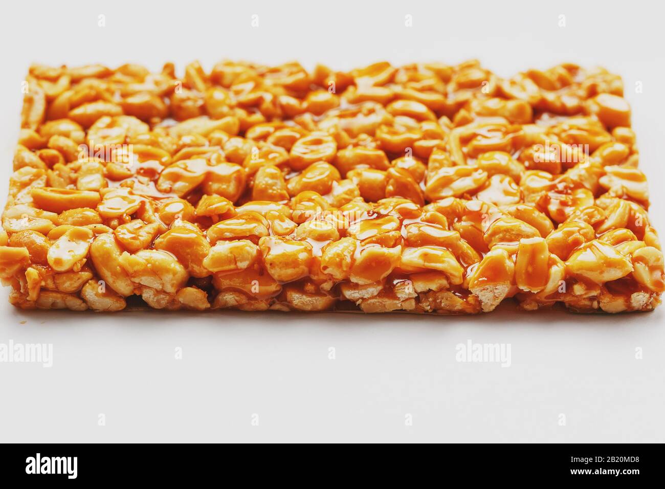 A large tile of roasted peanuts bar in a sweet molasses on a white ...