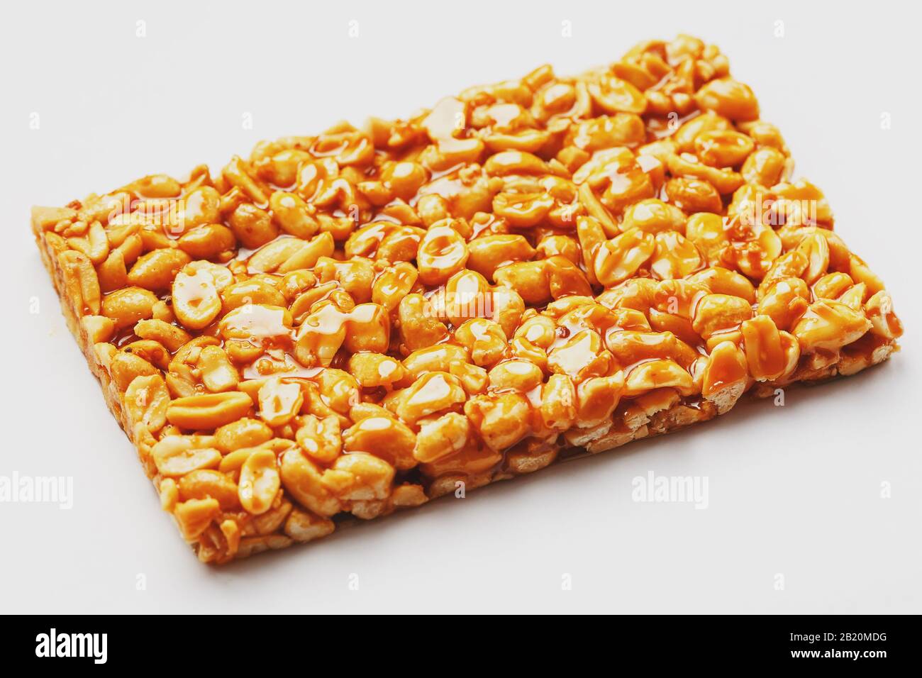 A large tile of roasted peanuts bar in a sweet molasses on a white ...