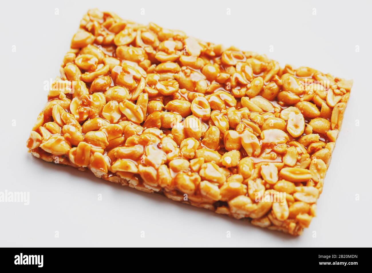 A large tile of roasted peanuts bar in a sweet molasses on a white ...