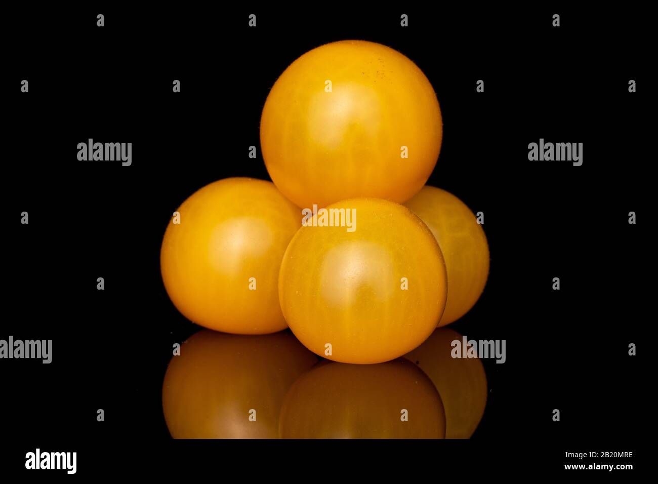 Group of four whole fresh yellow tomato stack isolated on black glass ...