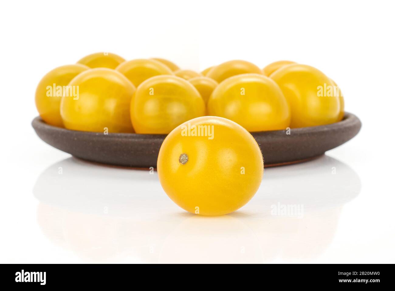 Lot of whole fresh yellow tomato with brown ceramic coaster isolated on ...