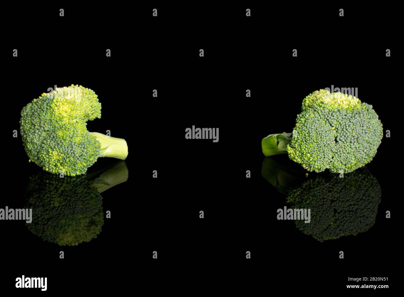 Group of two whole fresh green broccoli head isolated on black glass ...