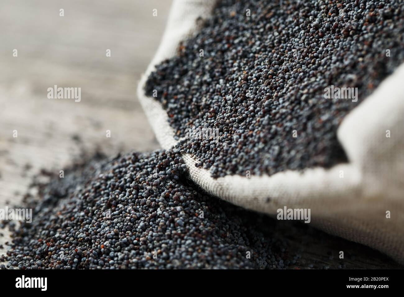 Poppy seeds in a burlap bag on a vintage wooden gray background. In ...