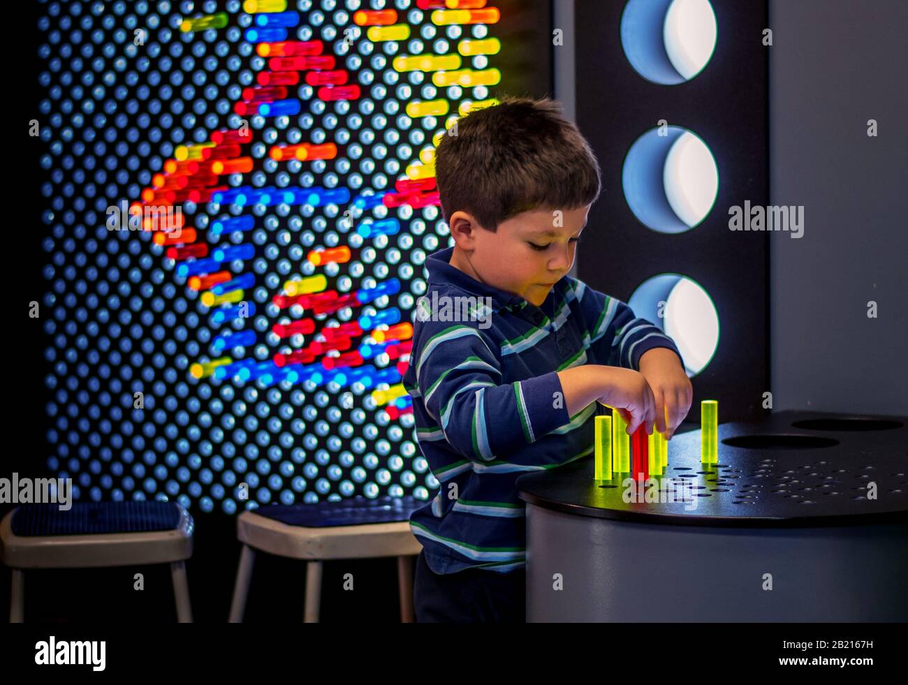 A young boy plays with colored acrylic pegs and a lit grid, to create ...
