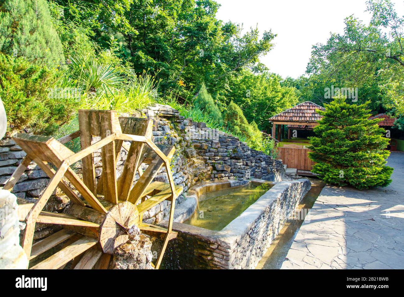 A water wheel on a stream lined with wild stone. Around greenery and ...