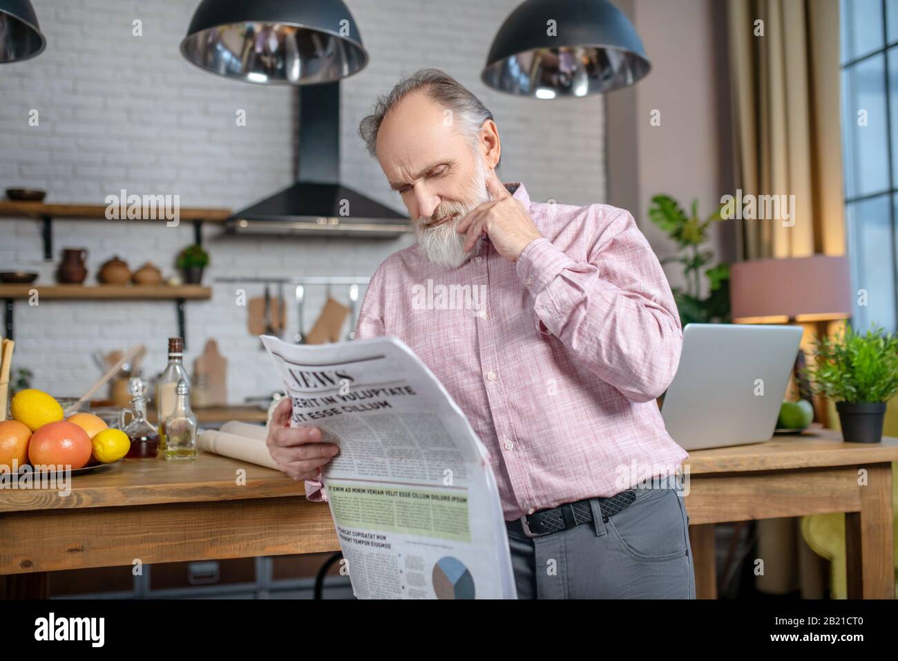 Thoughtful elderly man reading a newspaper in the kitchen Stock Photo ...