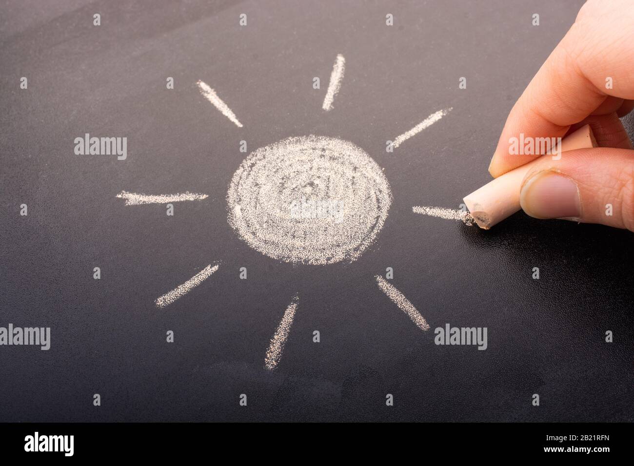 Hand drawing sun by chalk with light ray shape on blackboard background ...