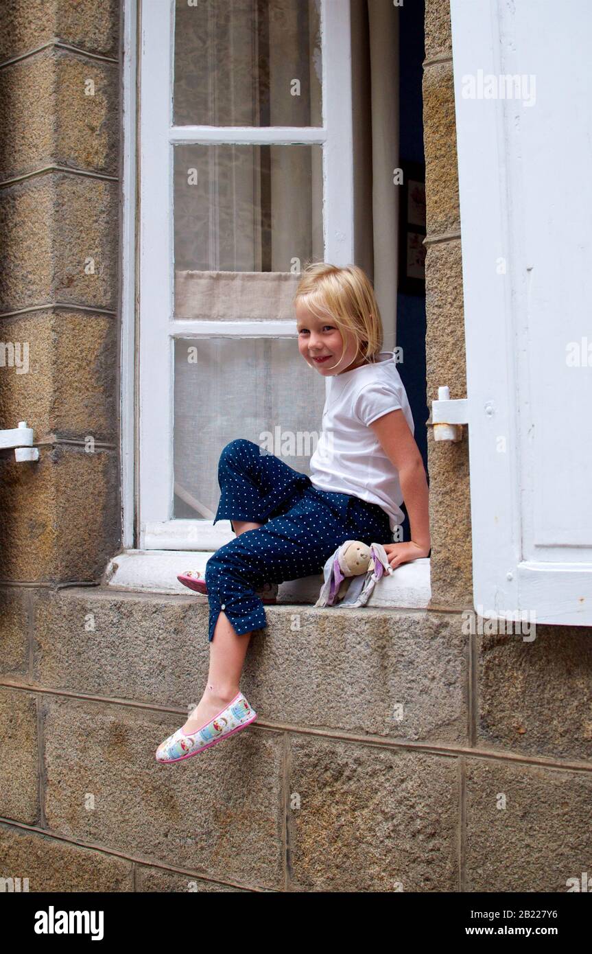 A little girl climbs out of the window of the house Stock Photo - Alamy