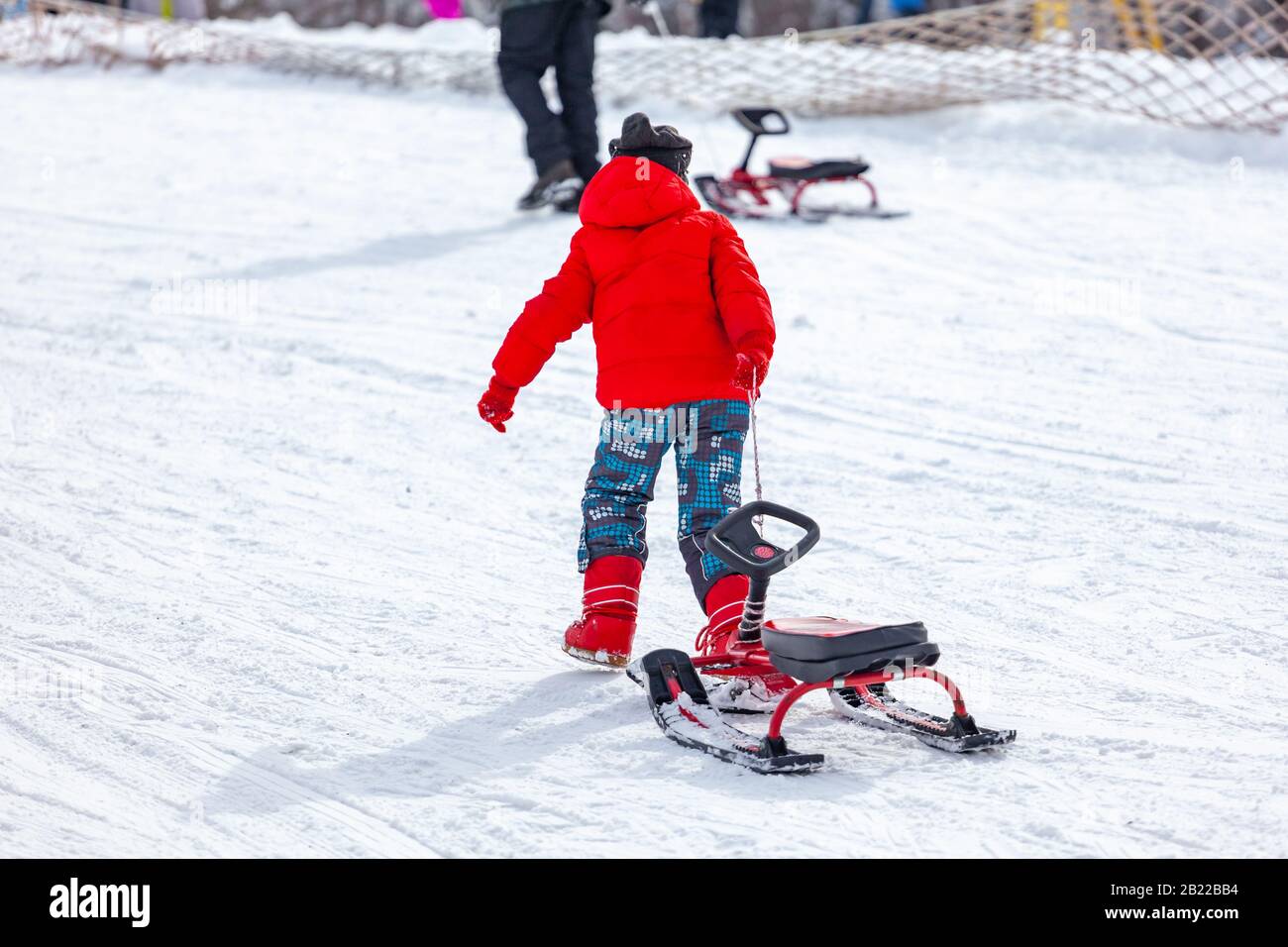 Back view of child in pulling sledge and running up snowy slope while ...