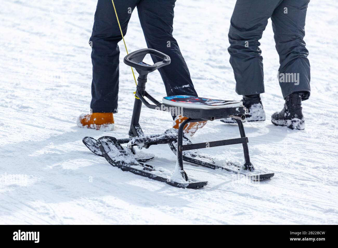 Back view of child in pulling sledge and running up snowy slope while ...