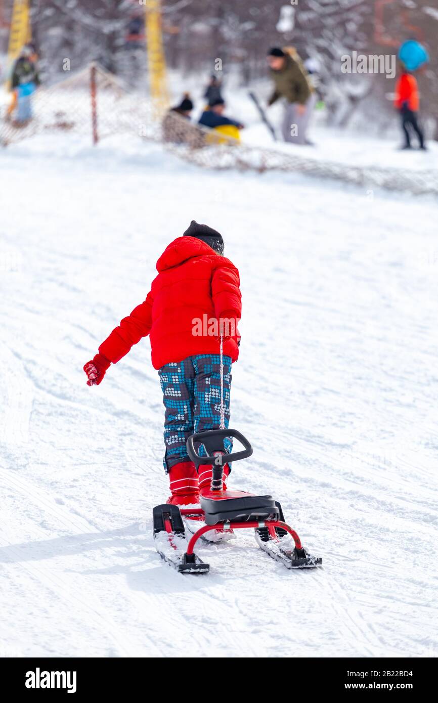 Back view of child in pulling sledge and running up snowy slope while ...