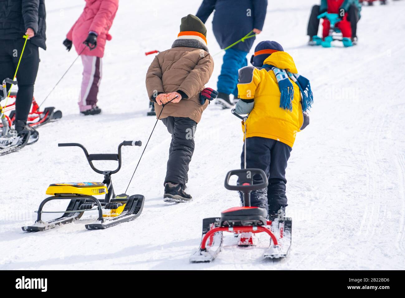 Back view of child in pulling sledge and running up snowy slope while ...