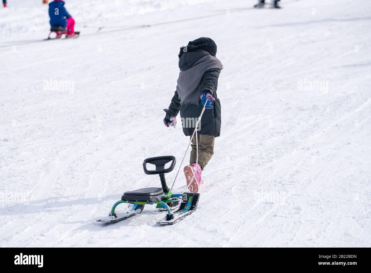 Back view of child in pulling sledge and running up snowy slope while ...